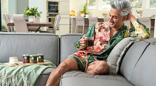 Tan France sitter och njuter av kaffe i blommiga shorts och skjorta